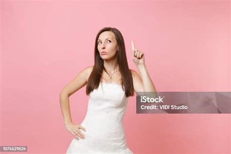 우아한 하얀 웨딩 드레스 서 포인팅 검지 손가락에 고립 된 파스텔 핑크 배경 최대에서 염려 엄격한 신부 여자의 초상화 결혼식 축 하 개념입니다 광고에 대 한 공간을 복사