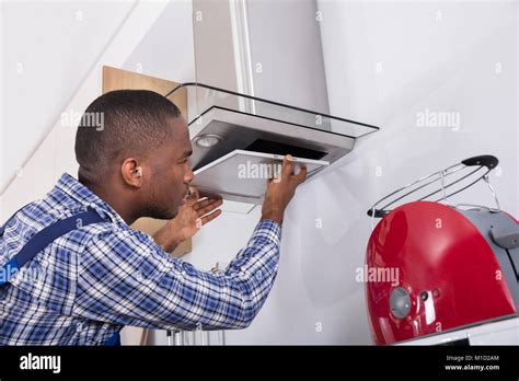 Young African Male Fixing Kitchen Extractor Filter In Kitchen Room