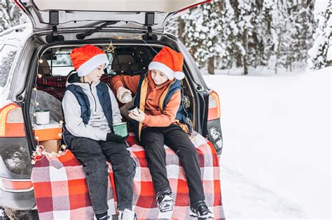 크리스마스를 위해 장식 된 자동차 트렁크에 보온병이있는 빨간 산타 모자를 쓴 두 친구 십대 소년 도로 여행 모험과 지역 여행 개념 눈 덮인 숲에서 겨울 피크닉 새해 휴가