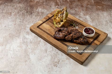 구운 필레미뇽 스테이크 세 조각이 나무 판자 위에 놓여 있습니다 근처에는 발사믹 소스를 곁들인 구운 양배추와 체리 소스를 곁들인