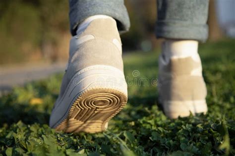Rear View Of Female Legs In Jeans And Sneakers Walking On Grass Stock