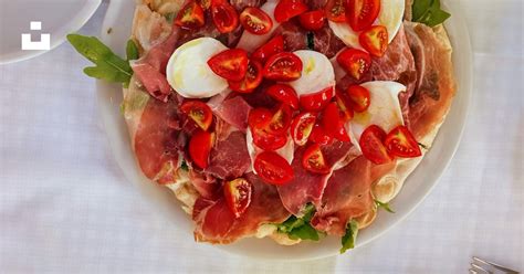 흰색 세라믹 접시에 얇게 썬 토마토와 녹색 잎 야채를 곁들인 피자 사진 Unsplash의 무료 음식 이미지