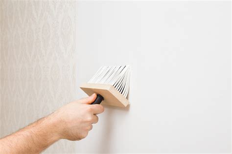 젊은 성인 남자 손 브러시를 사용 하 고 벽지에 대 한 흰색 벽에 접착제를 적용 근접 촬영 가정의 수리 작업 측면 보기입니다