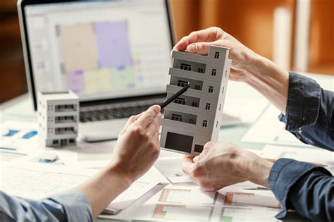 兩位建築師拿著房子模型和建築平面圖在桌子上擺著藍圖和筆記型電腦 照片檔及更多 人 照片 人 企業 住宅內部 Istock