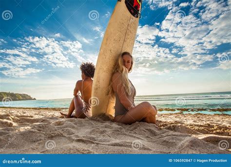 Девушки серфера смешанной гонки сидя спина к спине с Surfboard In