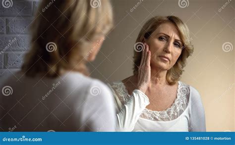 Depressed Elderly Woman Looking In Mirror Touching Wrinkled Face Lost