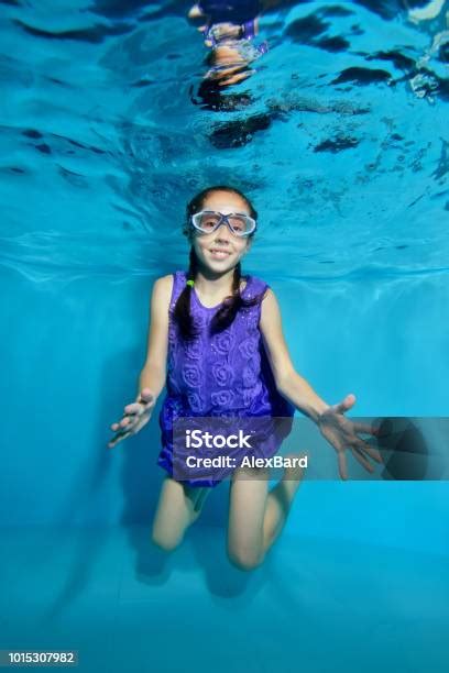 웬 수 중 수영 안경 보라색 드레스에 파란색 배경에 수영장에서 웃 고 포즈와 매력적인 작은 소녀 초상화입니다 수 중 사진입니다 세로 보기 건강한 생활방식에 대한 스톡 사진