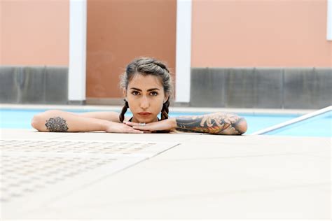 Young Woman With Tattoos Leaning On The Side Of A Swimming Pool · Free