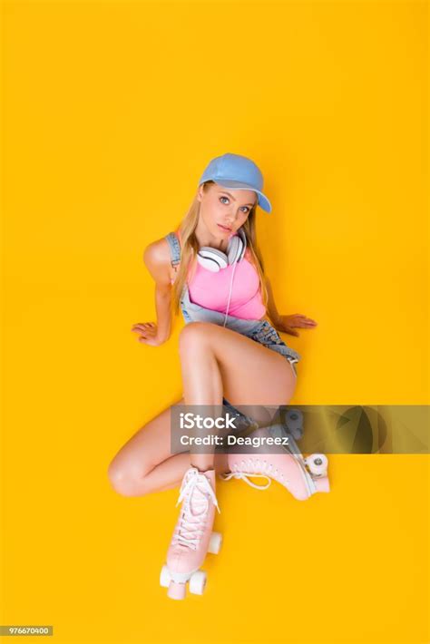 톱 보기 카메라 노란색 배경에 고립 된 보고 다리에 목 롤러 스케이트에 헤드셋으로 바닥 바닥에 앉아 멋진 모델 매혹적인 유혹 여자의 초상화 가냘픈에 대한 스톡 사진 및 기타