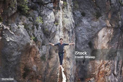 남자는 뻗어 슬링을 따라 걷고 있다 산에서 하이 라인 남자는 균형을 잡는 다 자연에서 줄 타기 워커의 성능 계곡의 배경에 높은 라이너 걷기에 대한 스톡 사진 및 기타 이미지