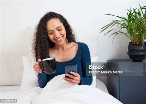젊은 다민족 여성이 침대에서 커피를 마시면서 휴대 전화에서 깨어납니다 20 24세에 대한 스톡 사진 및 기타 이미지 20 24세 Z세대 갈색 Istock