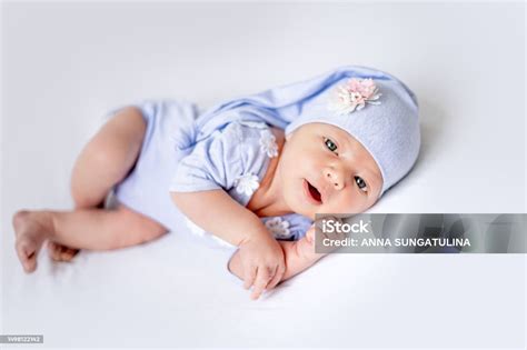 아름다운 파란색 바디 수트와 잠자는 모자를 쓴 갓 태어난 여자 아기가 하얀 배경에 눈을 뜨고 잠들거나 하품을하고 아기의 탄생 행복한 가정 1개월에 대한 스톡 사진 및 기타