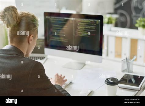 Back View Portrait Of Contemporary Young Man Coding At Modern Computer Sitting At Desk And