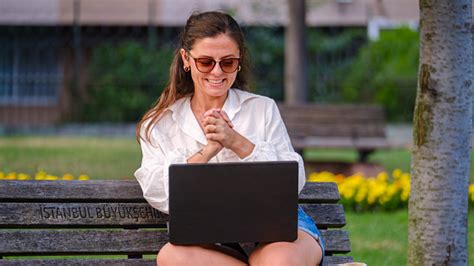 공원 벤치에 앉아 무릎 위에 올려놓고 노트북으로 작업하는 아름다운 중년 사업가가 성공에 대한 기쁨과 흥분을 명확하게 전달하는 몸짓과 표정을 보여주고 있습니다 35 39세에