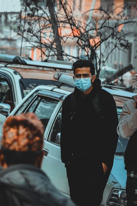 거리 검은 옷 까마귀 남자 보도 사람 서 있는 수직 쐈어 신호등 안면 마스크 정지 신호등 젖은 길 주머니에 손을 넣다에 관한 무료 스톡 사진