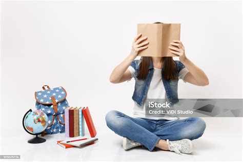 젊은 갈색 머리 여자 학생 데님 옷 책으로 얼굴을 덮고 글로브 책 가방 학교 책 흰색 배경에 고립 가까이 앉아 읽고 고등학교