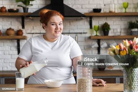 부엌에서 우유와 귀리 조각으로 만든 건강한 아침 식사를 요리하는 쾌활한 백인 여성 플러스 크기 통통 한 여자 다이어트 에 대 한 스포티 한 모양과 체중 감량 남자에 대한