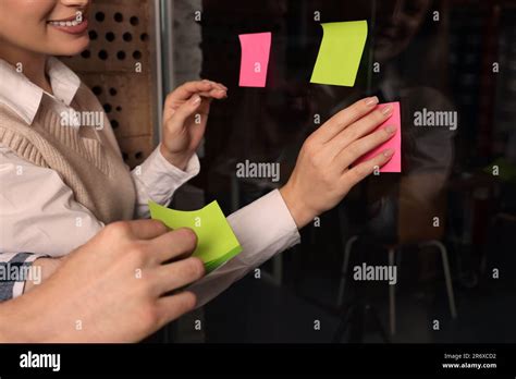 Employees Putting Colorful Sticky Notes On Glass Door In Office