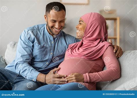 Happy Expecting Muslim Couple Relaxing Together On Sofa In Living Room
