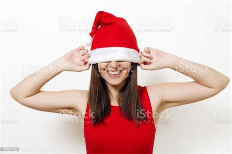 아름 다운 백인 젊은 행복 한 여자 건강 한 피부와 빨간 드레스와 흰색 바탕에 그녀의 눈을 덮고 크리스마스 모자를 입고 매력적인 미소 산타 소녀 격리입니다 새 해 휴일