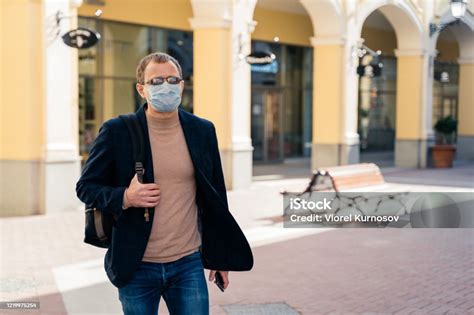 코로나바이러스와 전염병이 있는 동안 유럽 남자는 보호 용 얼굴 마스크를 착용하고 배낭을 운반하고 버스 정류장에서 야외에서 포즈를 취하고 검역 중에 여행합니다 코비드19
