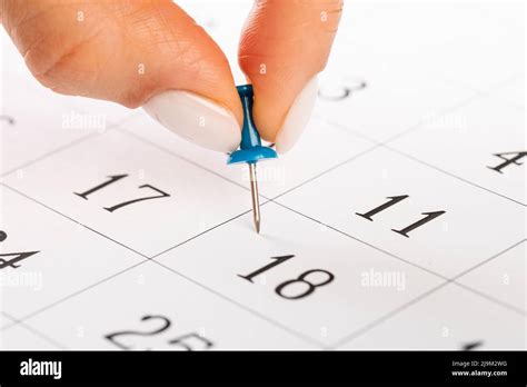 Beautiful Female Hand With Manicure Pushes A Blue Pin On A Calendar