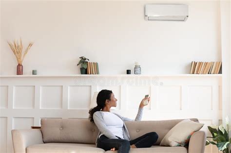 Happy Young African American Woman Turning On Air Conditioner Stock