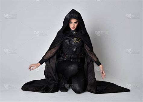 一个红头发、身穿深色皮革刺客服装、身穿黑色长斗篷的女人的幻想画像。全长跪姿，与工作室背景隔离