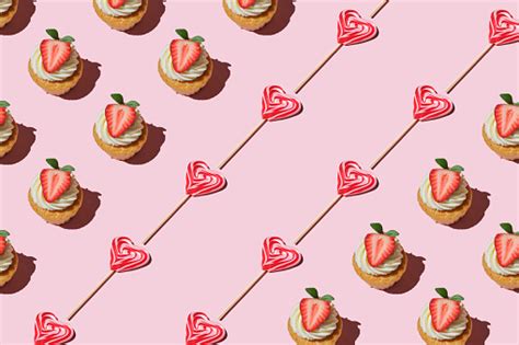 분홍색 배경에 딸기와 하트 모양의 롤리팝홈 쿠키로 만든 패턴 위에 큰 딸기와 컵 케이크 빨간색과 Whie 줄무늬 달콤한 롤리팝 플랫 레이 스타일 축제 배경 냉동식품에 대한