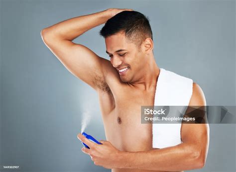 남자 미소를 짓고 스튜디오의 피부에 데오도란트를 뿌려 향기 위생 및 신선한 향기를 만드십시오 모델 회색 배경에 겨드랑이에서 땀