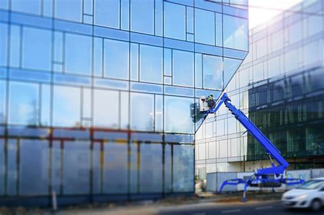 사무실 유리 건물과 노동자 높은 리프팅 플랫폼에서 작업 크레인 및 유리 수리를 위한 준비 설치 건물과 자동차에 반사되는 푸른 하늘과 태양이 지나가는 건물 정면에 대한 스톡