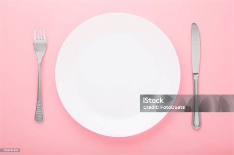 밝은 분홍색 테이블 배경에 포크와 칼 흰색 접시 파스텔 색상입니다 근접 촬영 식사 대기 개념입니다 하향하 보기 건강한 식생활에