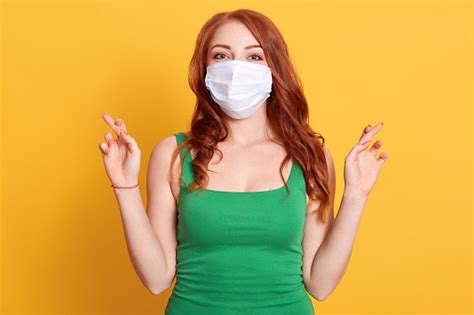 손가락이 달린 아가씨는 노란 배경에 가장 잘 어려워졌고 빨간 털이 많은 생강 여성이 불행하고 의료 용 마스크를 쓰고 질병으로부터