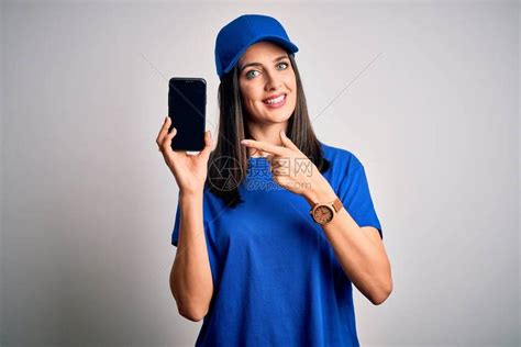 蓝眼睛戴着帽子拿着智能手机的年轻送货员非常高兴地用高清图片下载 正版图片504086130 摄图网