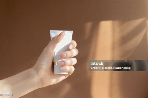 여성의 손은 손바닥에 흰색 표시가없는 크림 병을 클러치 바디 로션 세면도구가 있는 용기 햇빛의 광선에 갈색 배경에 전문 케어