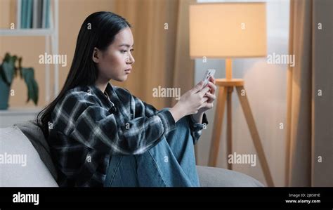 Side View Of Sad Bored Asian Woman Girl Sitting On Sofa At Home With