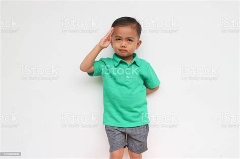 흰색 배경에 고립된 카메라를 보면서 군대처럼 경례를 하는 진지한 얼굴을 가진 귀여운 아시아 소년의 초상화 2 3 살에 대한 스톡