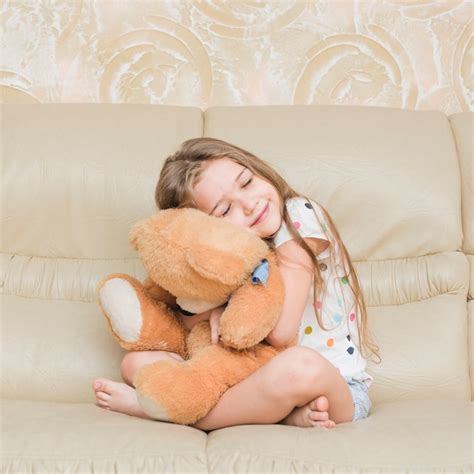 Premium Photo Smiling Girl Cuddling Her Teddy Bear Sitting On Sofa