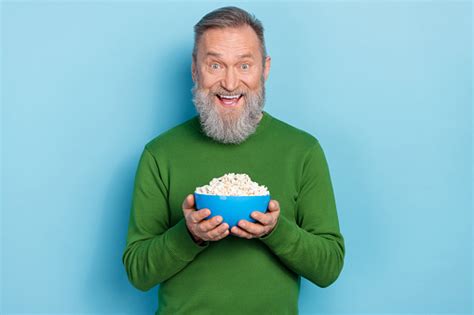 놀란 노인 홀드 플레이트 그릇 팝콘 주말 시계 시리즈 착용 점퍼 절연 블루 컬러 배경의 사진 60 64세에 대한 스톡 사진 및
