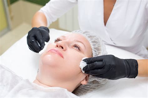 미용사 사무실에서 소파에 있는 의료용 모자에 누워 있는 한 젊은 여성의 초상화가 미용 시술 중 환자의 얼굴에서 면 패드로 과도한