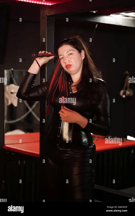 Sensual Woman In Black Latex Costume With Leather Whip In Bdsm Room