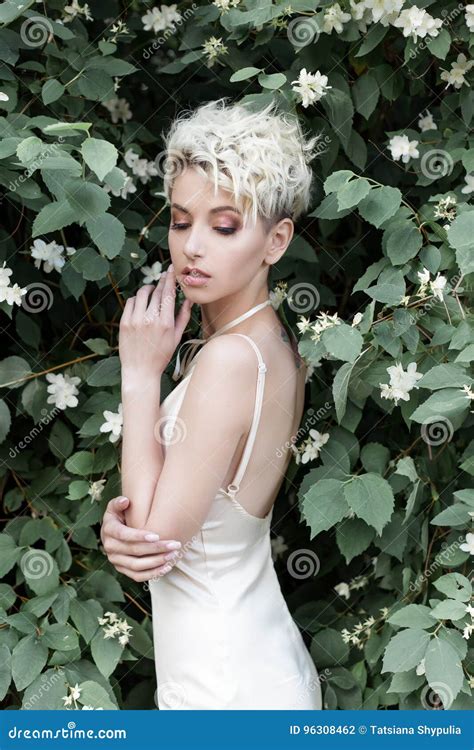 Красивая сексуальная нежная девушка с короткой стрижкой в Cream платье с цветком жасмина