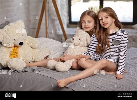 The Image Of Two Little Sisters Sitting On The Bed In The Room Stock