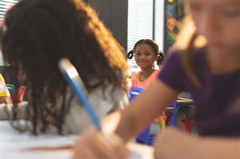 Colegiala mirando a la cámara mientras está sentado en el escritorio en la escuela Foto Premium