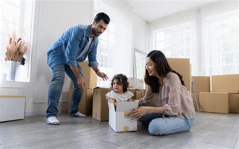 딸은 아빠와 엄마와 놀고있는 판지 종이 상자에 앉아 있습니다 그 가족은 방금 새 집으로 이사했습니다 부모와 아이들은 함께 물건을 정리하는 재미를 가지고있다 가족에 대한 스톡