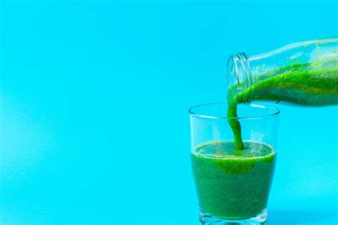 잎이 많은 녹색 야채 과일에서 녹색 신선한 스무디의 유리 병에서 따르기의 과정 밝은 파란색 배경에 사과 바나나 키 위 호박