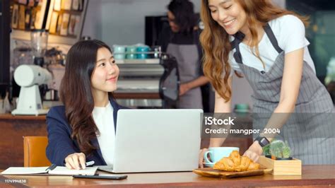 젊은 아시아 여자 바리스타 제공 A 커피 컵 와 미소 에 사업가 고객 동안 그녀 작업 에 노트북 컴퓨터 에 카페 커피 숍 배경 웨이트리스에 대한 스톡 사진 및 기타 이미지