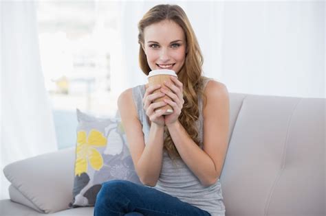 Premium Photo Smiling Young Woman Sitting On Couch Holding Disposable Cup
