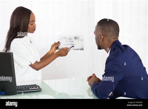 African American Woman Dentist Showing X Rays To Patient In Diagnostic