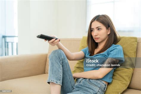 프로그램 메뉴를 바꾸기 위해 리모컨을 사용하여 텔레비전을 보는 행복한 젊은 아시아 여성 매우 즐겁고 흥분되는 Tv 메뉴 거실에